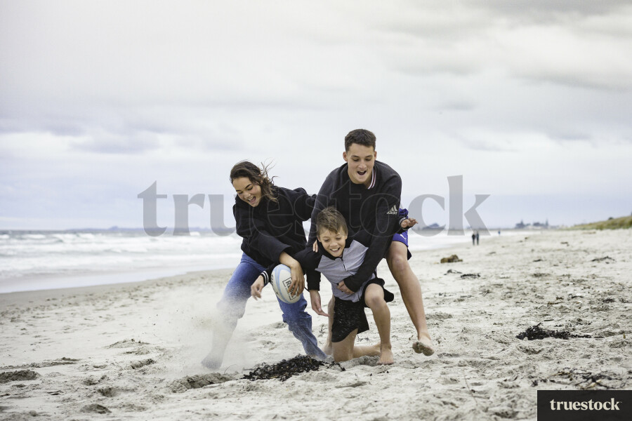 Whānau Playing Rugby at the Beach by Jay Drew - Truestock